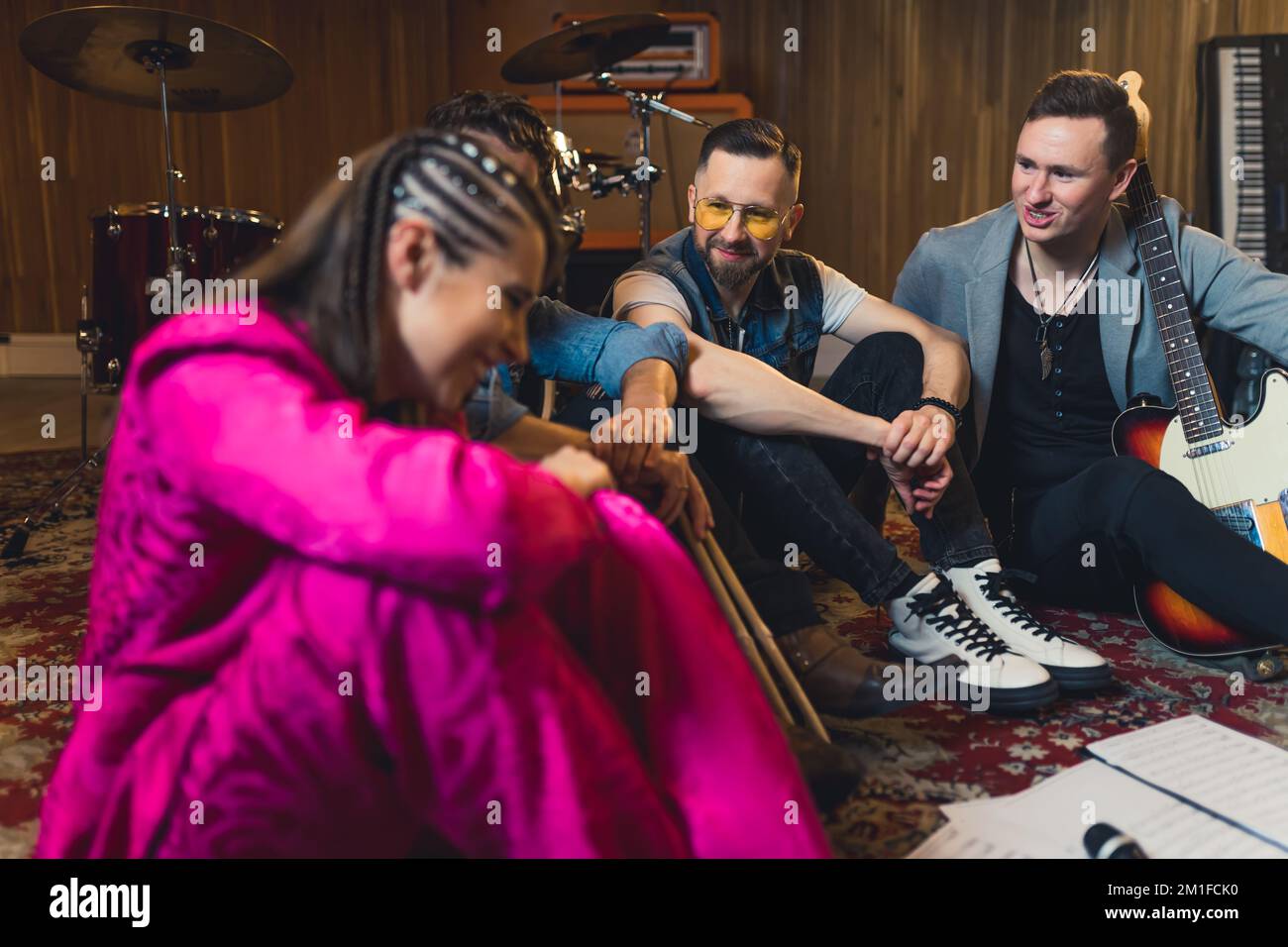 two guitarists, a drummer and a singer on the floor discussing about ...