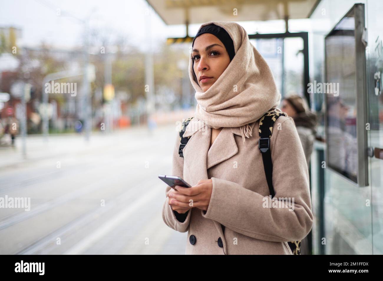 Young muslim woman with smartphone waiting for bus at city bus stop ...