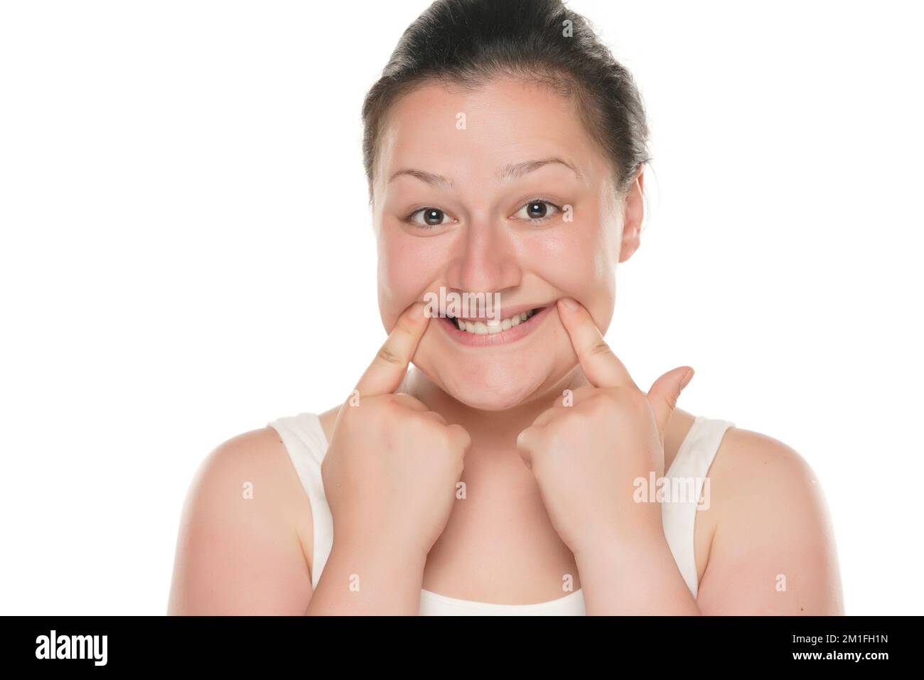 Young chubby woman forcing her smile with her fingers on white studio ...