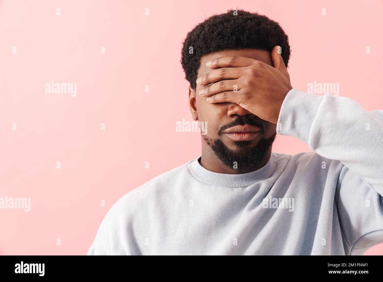 Black mid man with beard covering his eyes while posing on camera ...