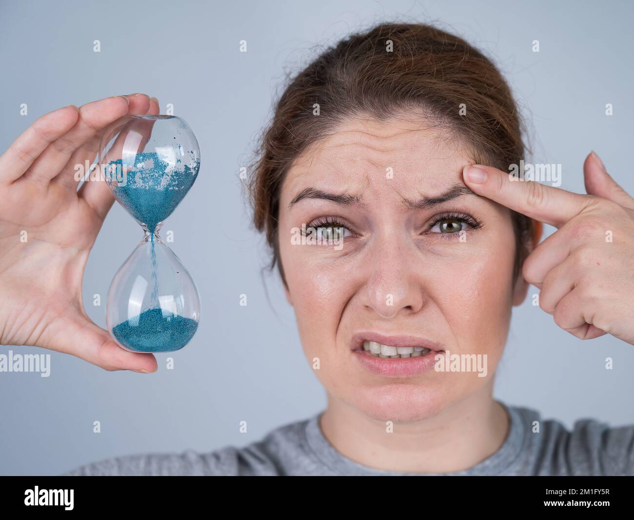 Unhappy caucasian red-haired woman looks at the hourglass and points to ...