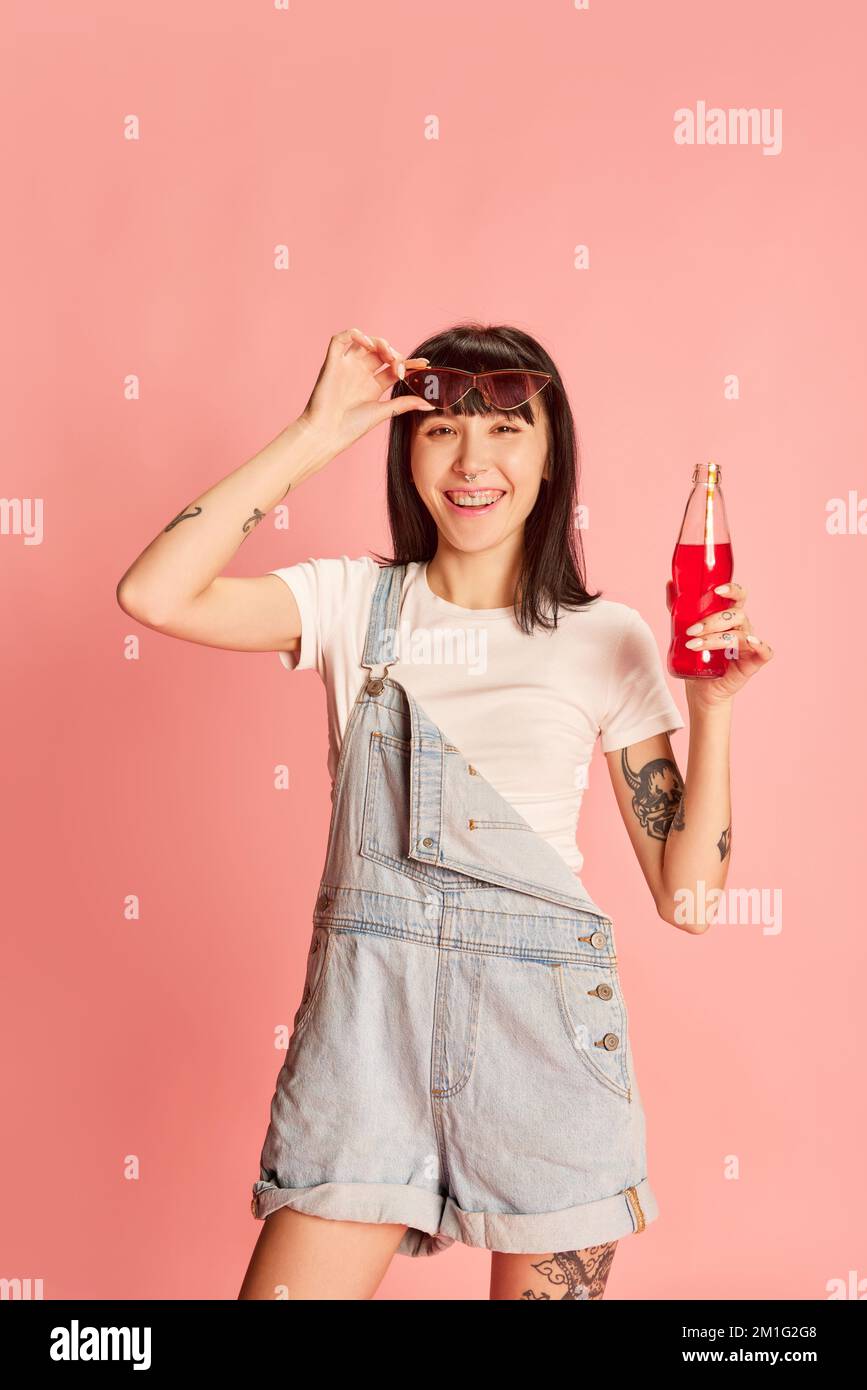 Young stylish girl posing in denim overalls, holding soda and ...