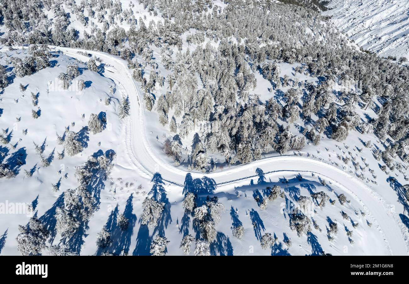 Drone aerial of a frozen road crossing a snowy forest mountain in ...