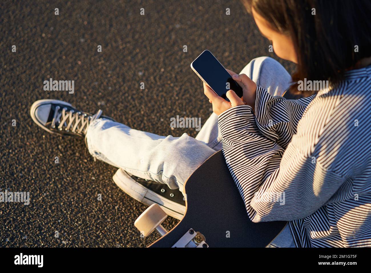 Close up of skater teen girl sits on skateboard, types message on ...