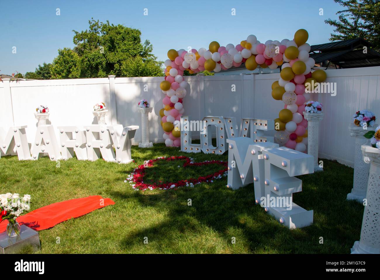 A backyard set up for a marriage proposal with a red carpet and letters ...