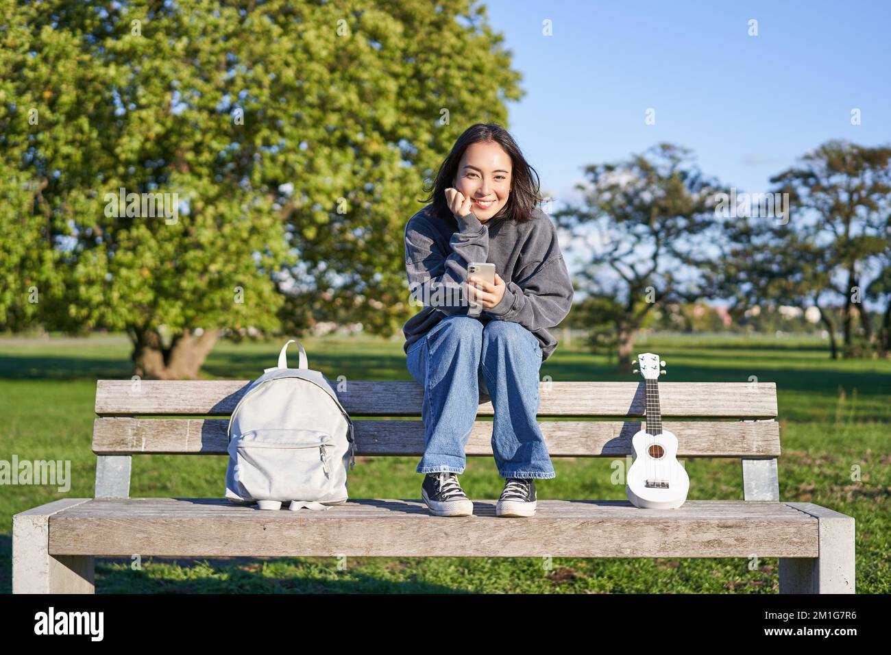 Beautiful brunette girl on bench in park, sitting with ukulele and ...