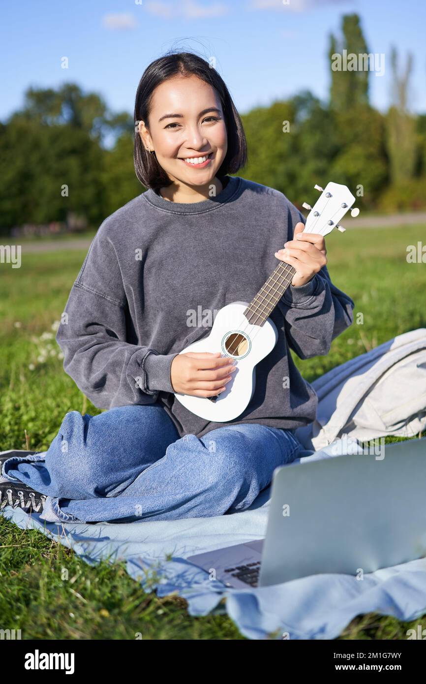 Cute korean girl, musician sits in park, plays ukulele and sings, looks ...