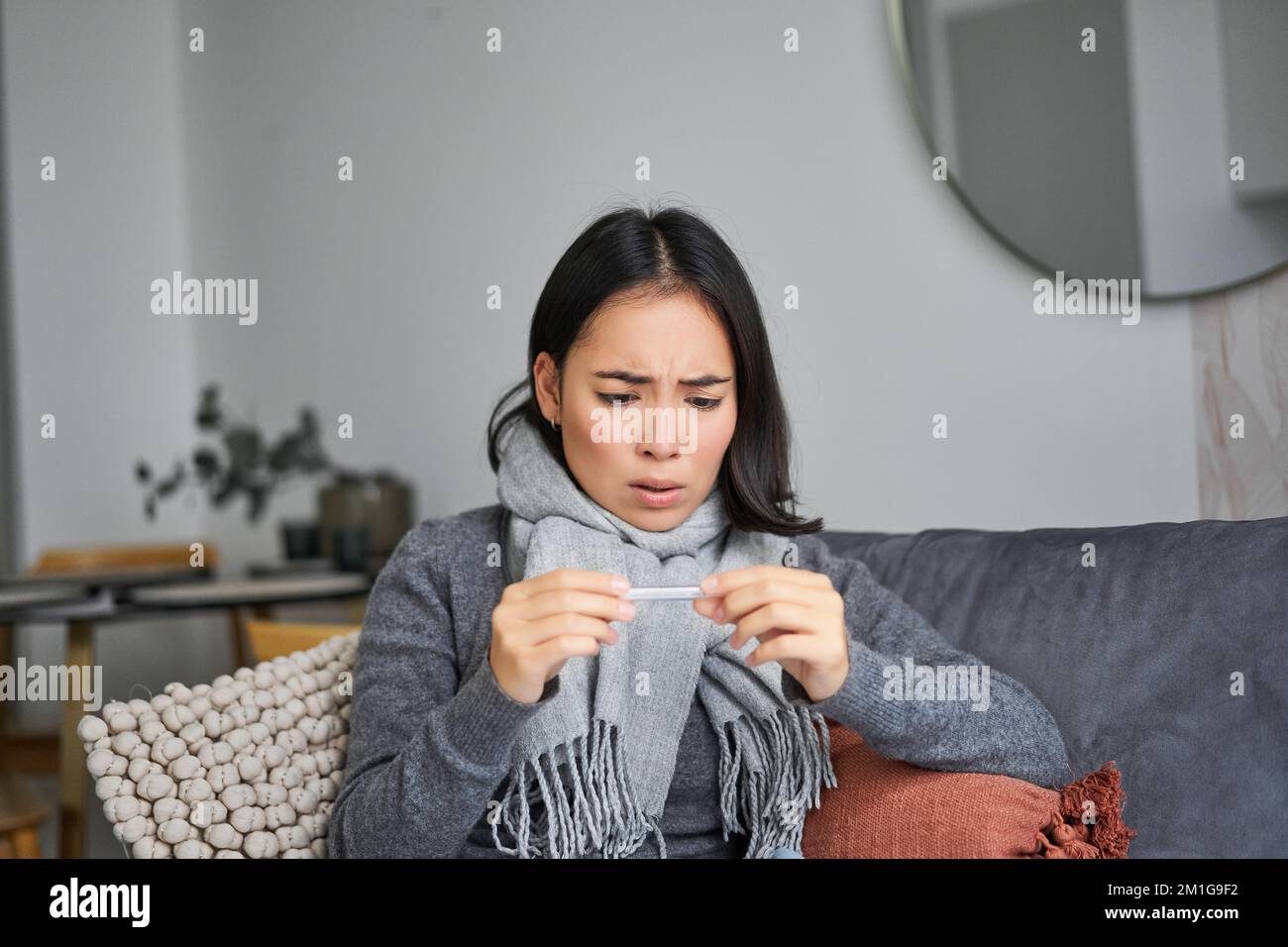 Shocked woman looks concerned at her thermometer, catching cold, has ...