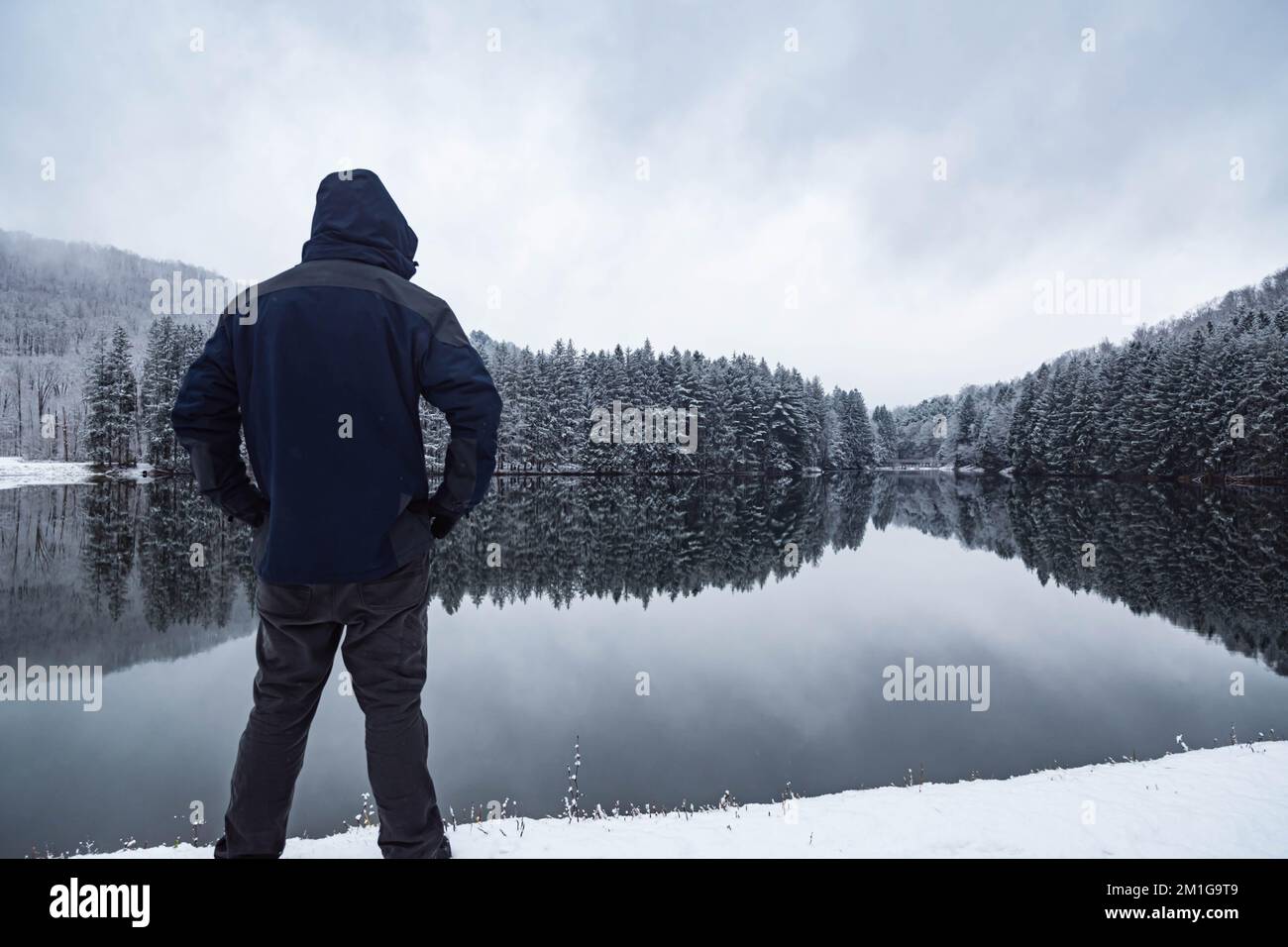 Hiker standing by a mountain lake during fresh snow fall, felling of ...