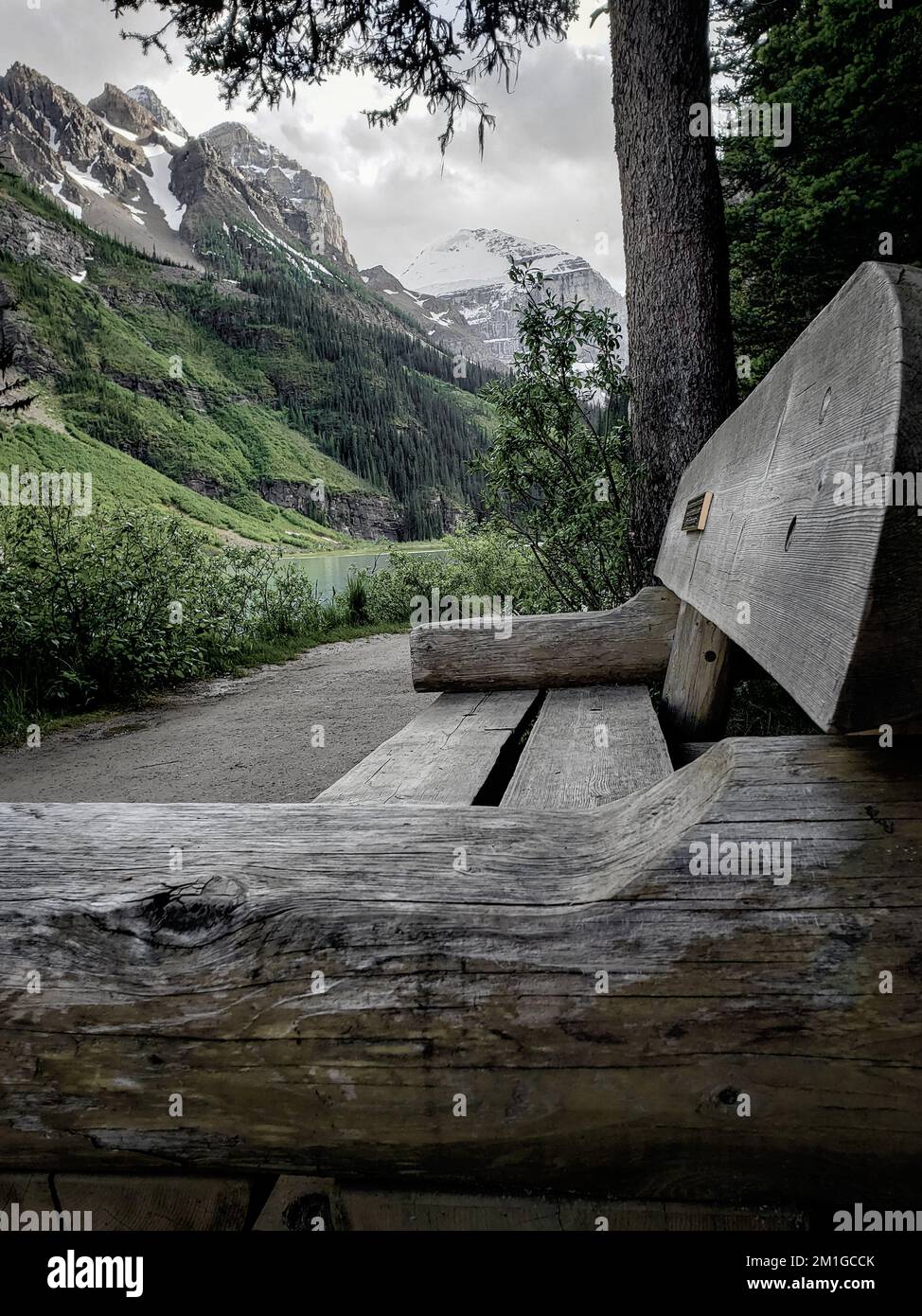 A vertical shot of a wooden bench near Lake Louise in the mountains of ...
