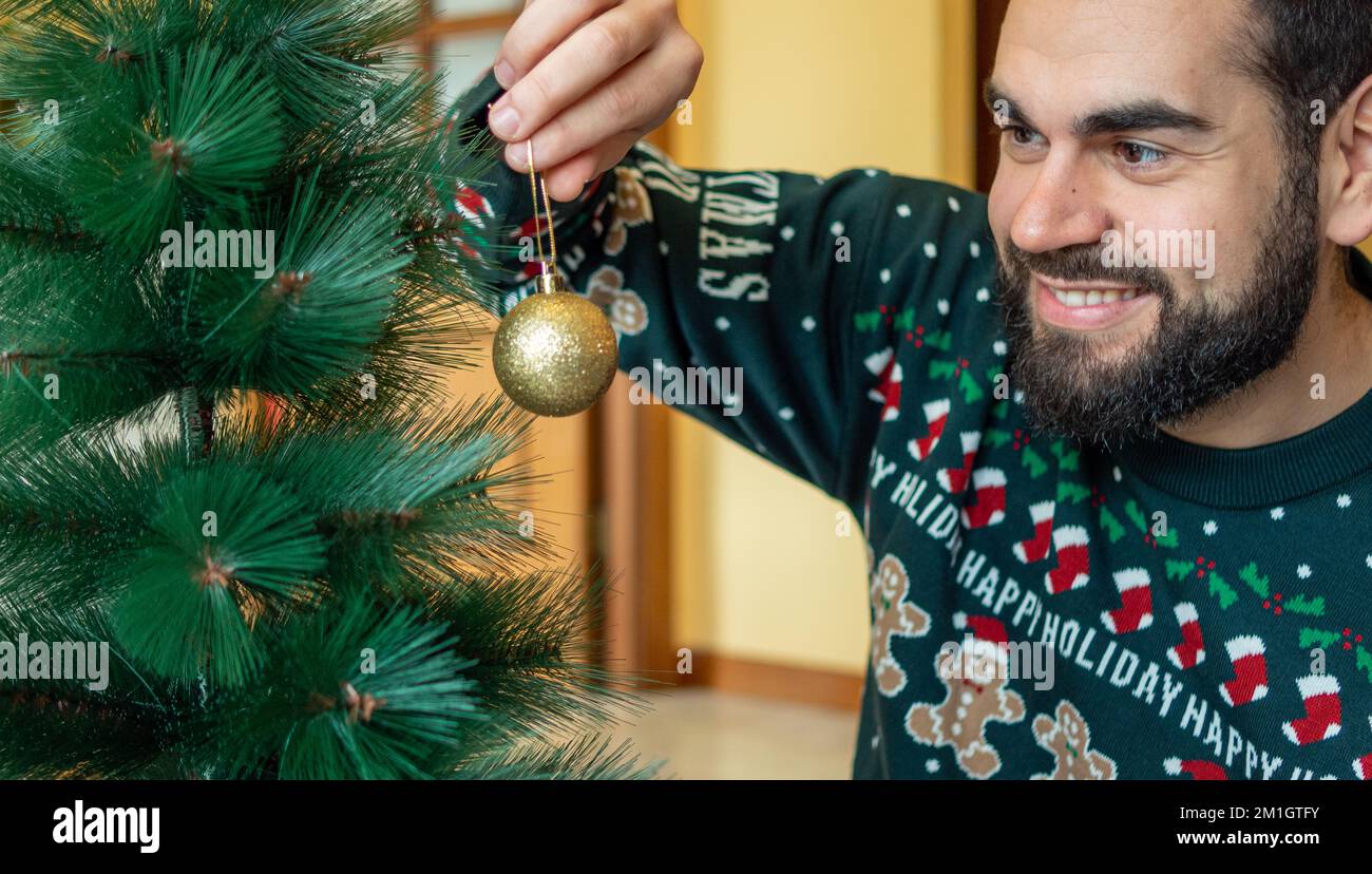 happy man putting a golden ball on the christmas tree wearing a ...