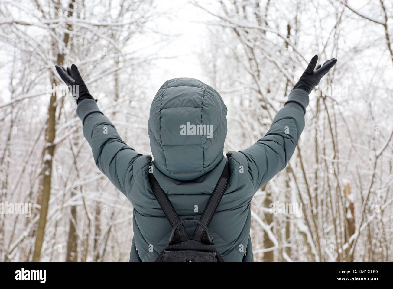 Woman wearing down jacket with hood standing with her hands raised and ...