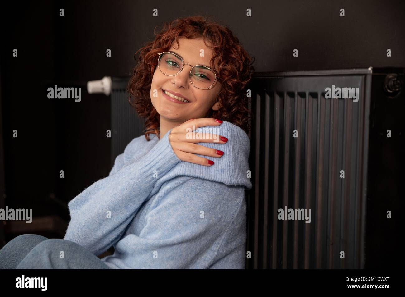 A smiling girl sits and leans against a hot radiator Stock Photo - Alamy