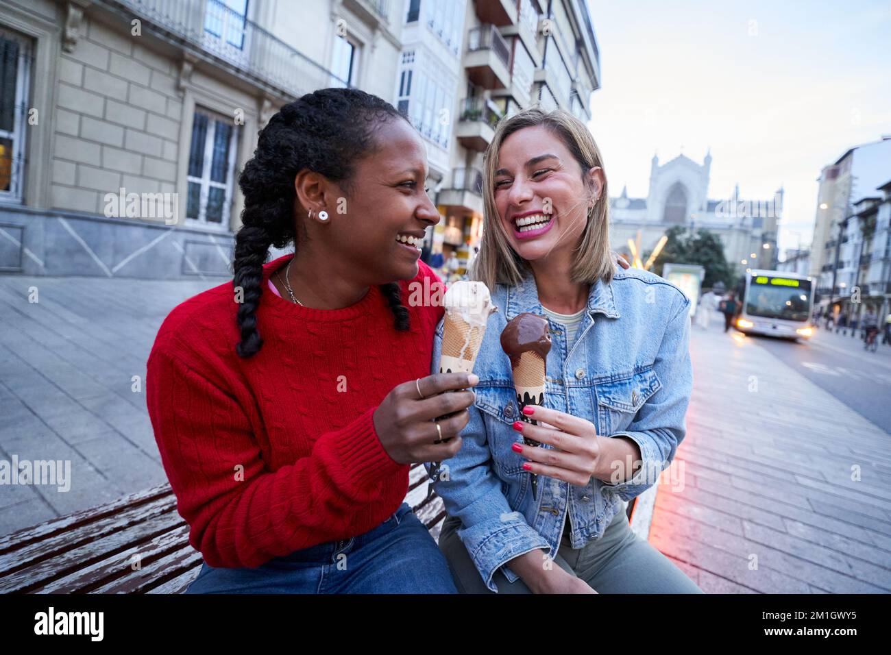 Young women sitting outdoors eating Ice cream on the street, enjoying ...