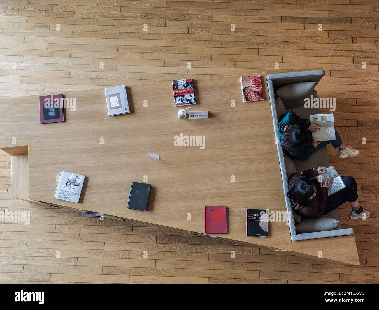 A top view of a wooden library table with seats and people sitting and ...