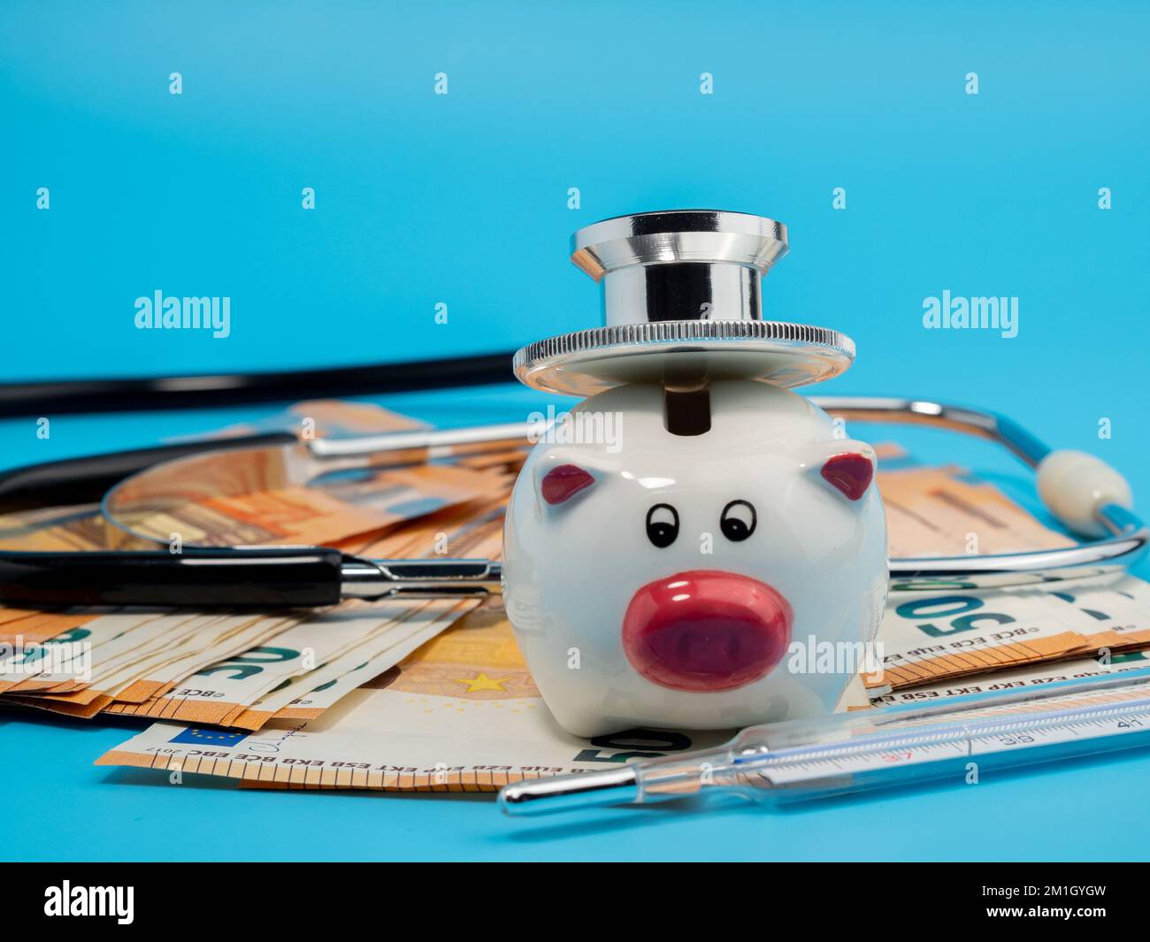 Medical stethoscope, piggy bank, thermometer and banknotes on a blue ...