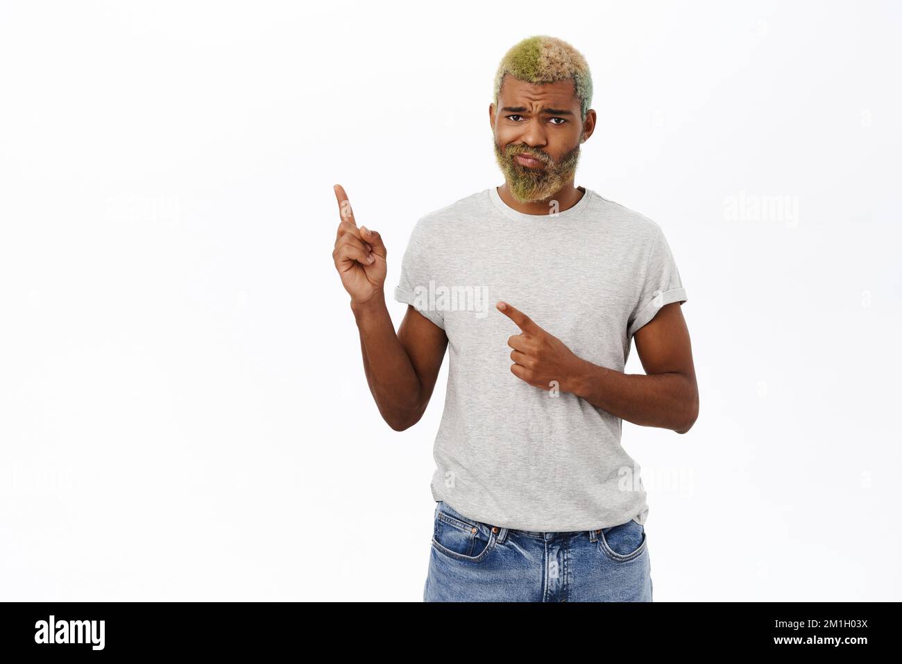 Upset hipster guy with yellow beard and hair, points left, frowns and ...