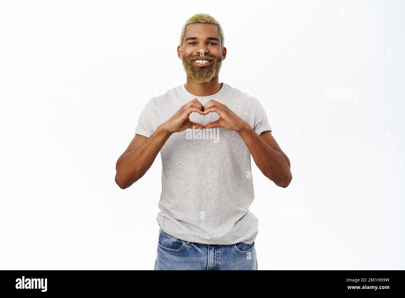 Smiling handsome guy shows love and care gesture, makes hand heart and ...