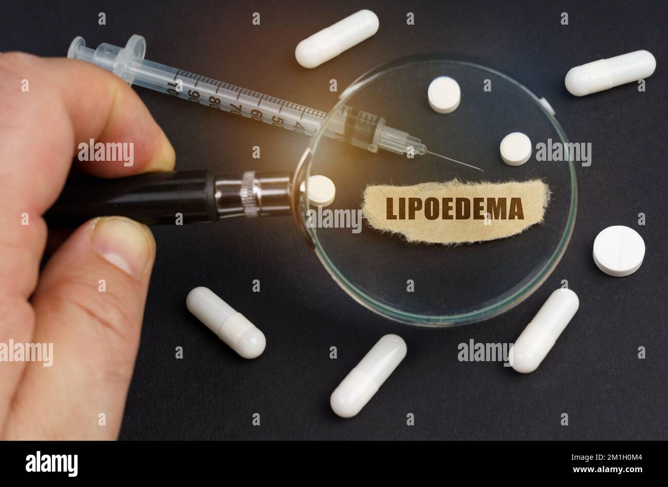 A man looks through a magnifying glass at pills, a syringe and a piece ...