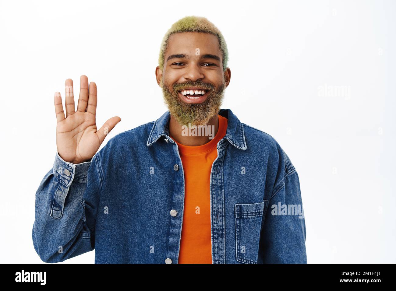 Close up of friendly stylish man waves hand, smiles and says hello, hi ...