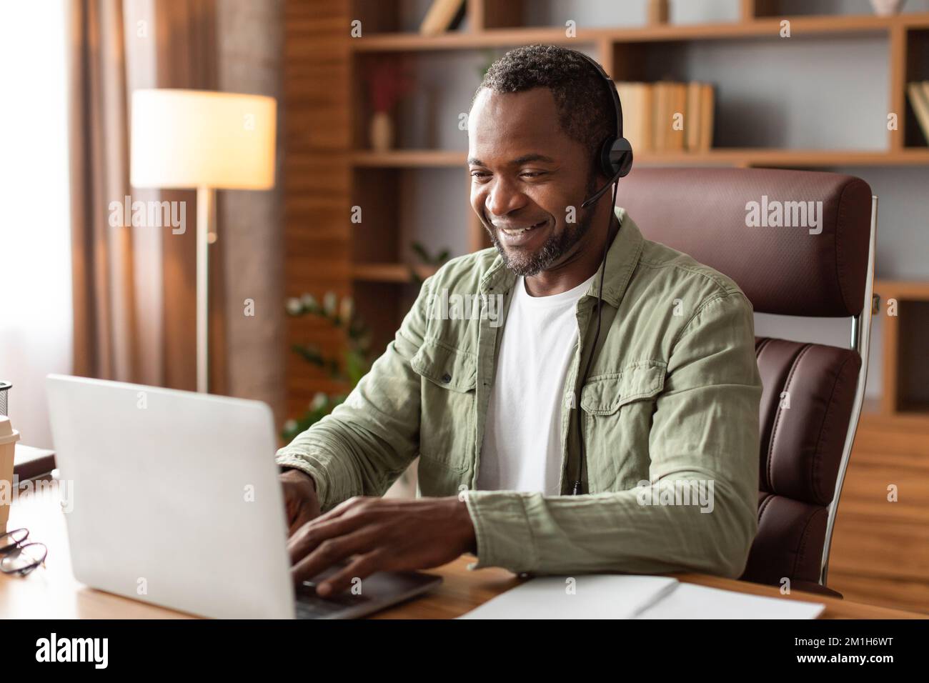 Happy successful adult black businessman in headset typing on computer ...