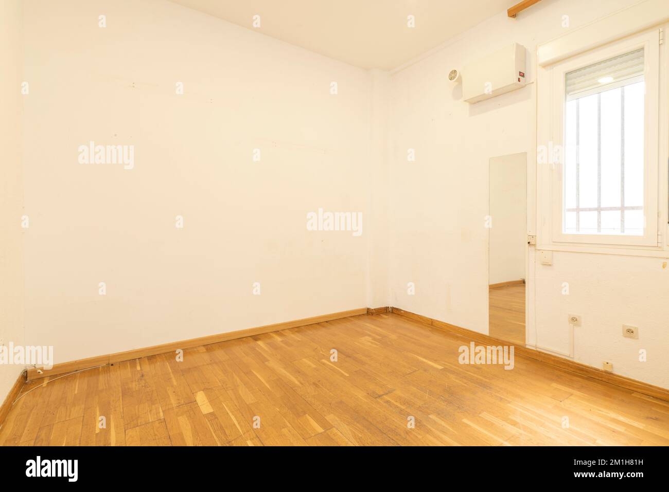 An empty room with a frameless mirror on the wall, worn wooden floors ...