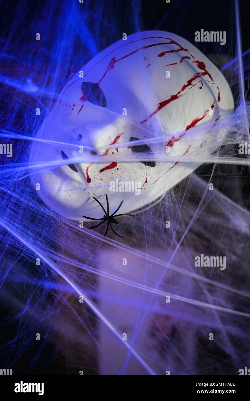 Color image of a white mask, painted with blood, in some spiderwebs and ...