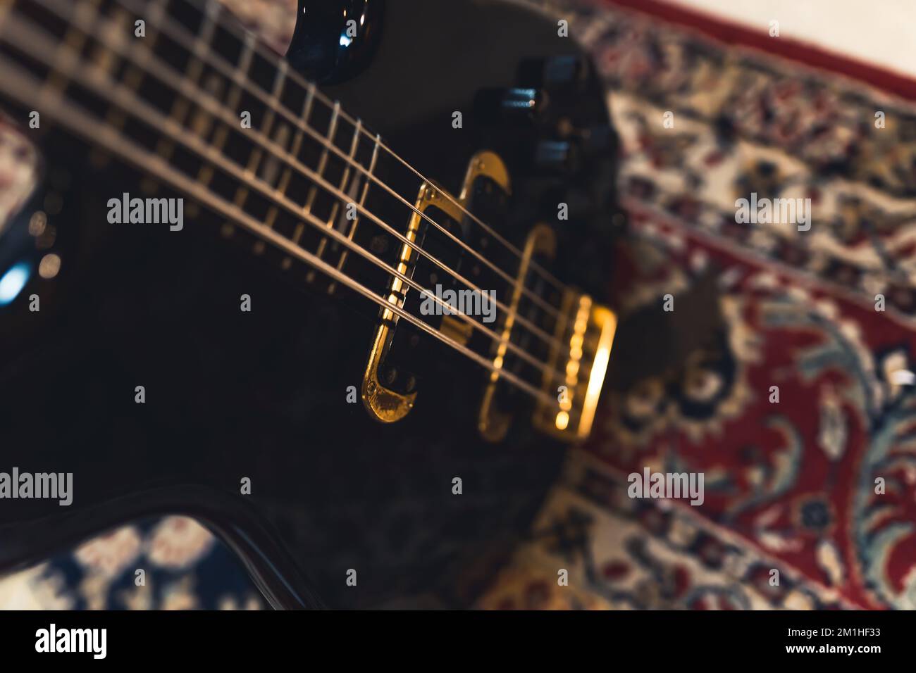 closeup shot of a black bass guitar with golden strings on the carpet ...