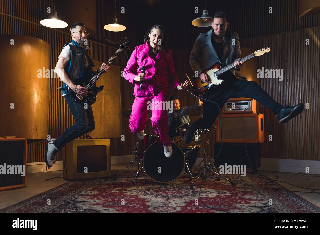 full shot of a young singer-woman and two guitarists jumping in the air ...