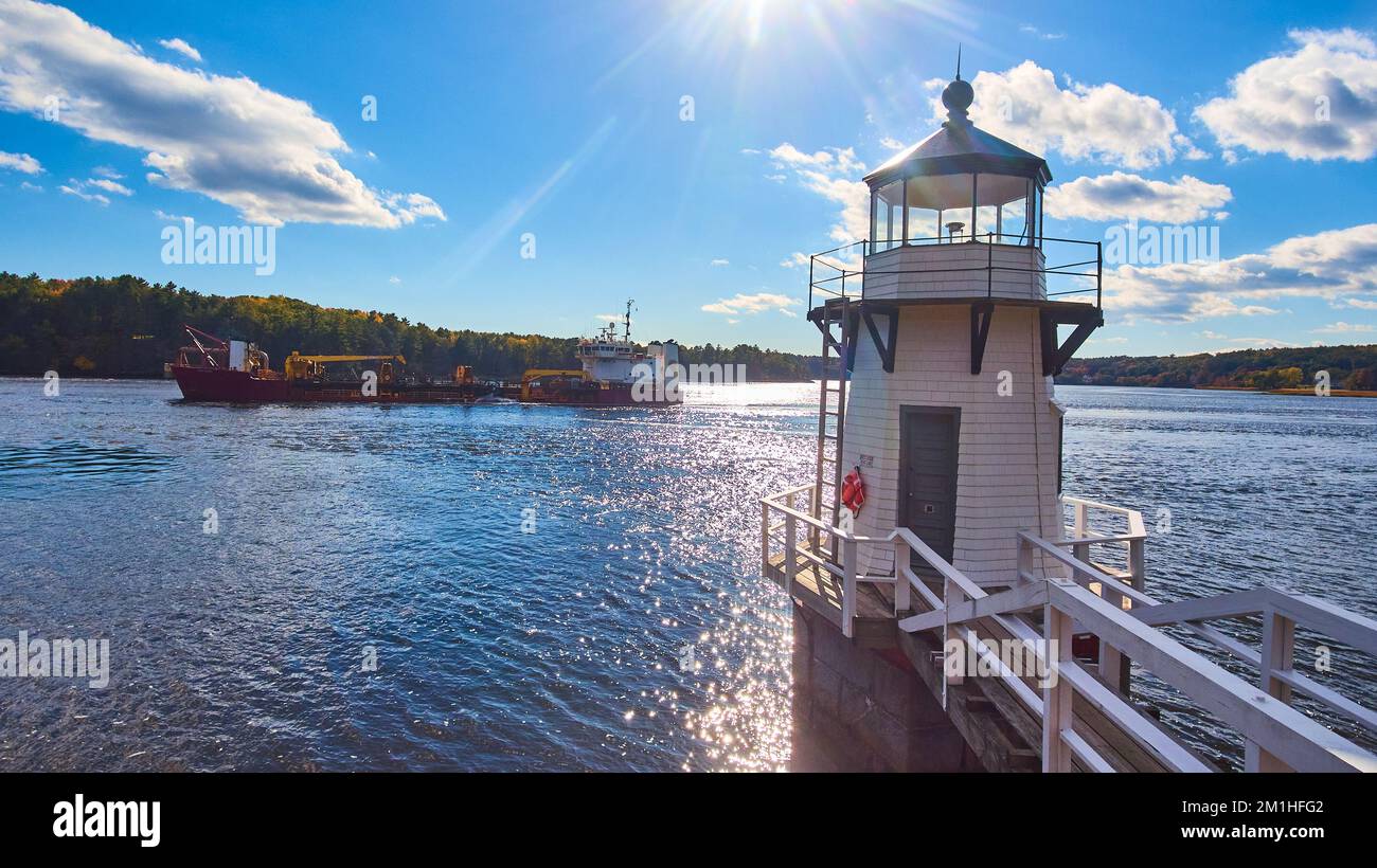 Large commercial ship on Maine river sails past small lighthouse with ...