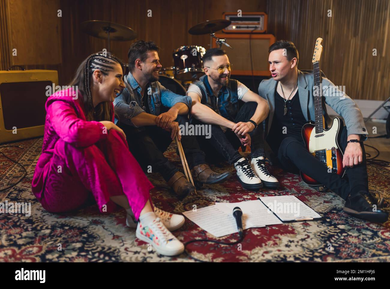 music band members sitting on the floor and talking cheerfully, drums ...