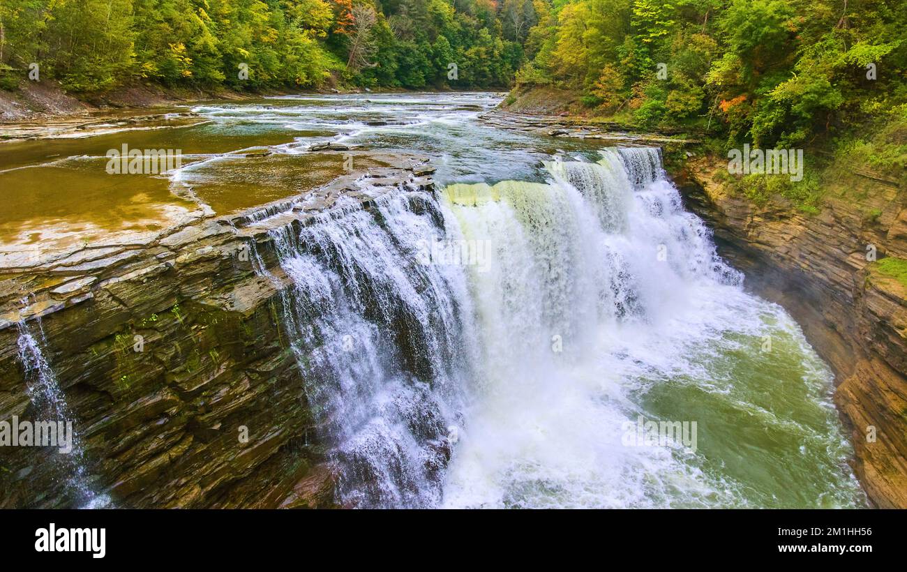 Aerial along edge of huge raging waterfall pouring over cliffs ...