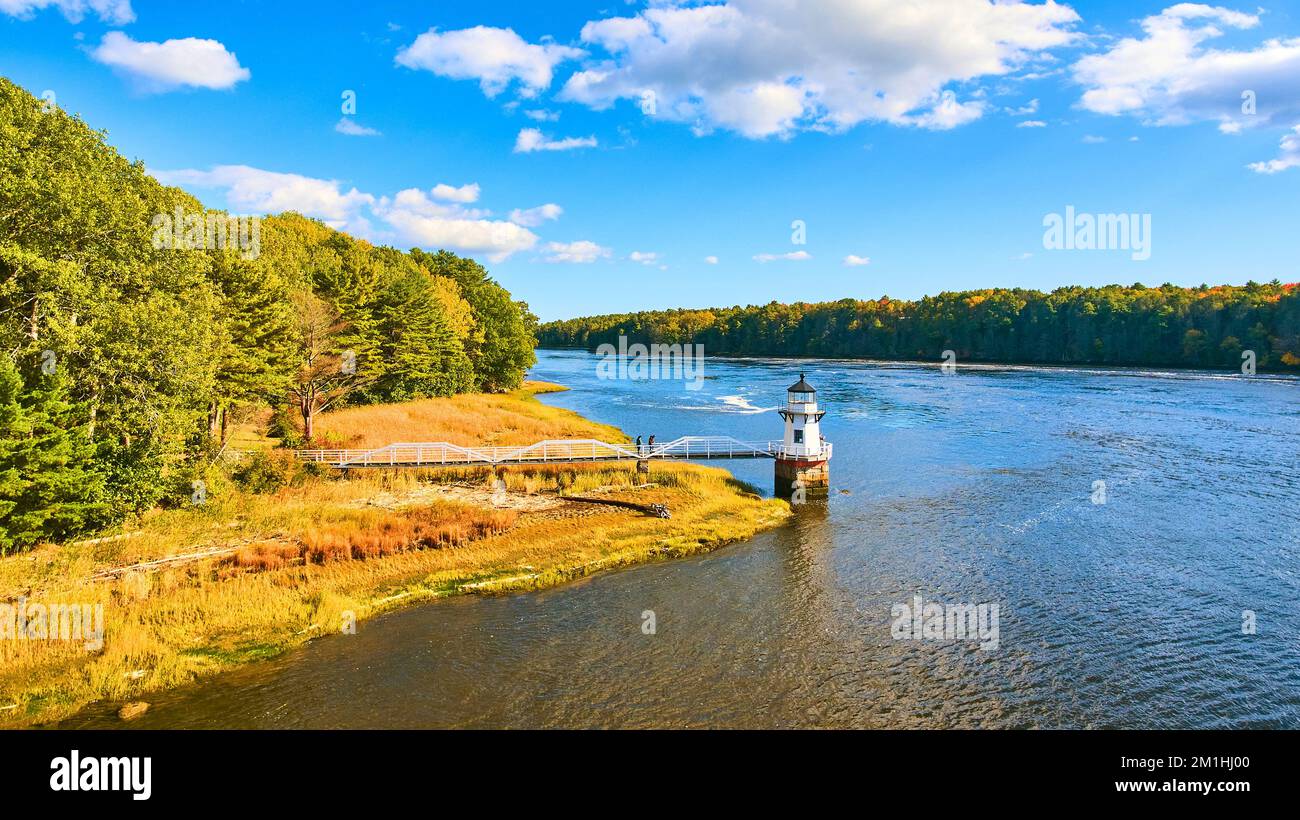 Warm light shines over small lighthouse from aerial view with fall ...