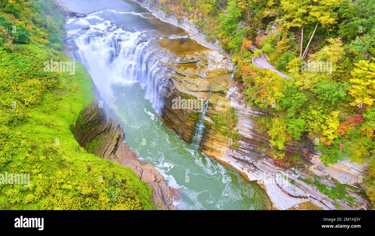Aerial over stunning raging waterfalls eroding cliffs with lush ...