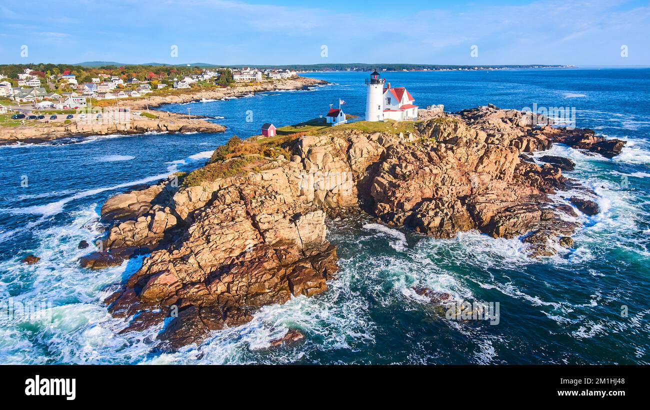Waves crash over rocks aerial over Maine island with lighthouse and ...