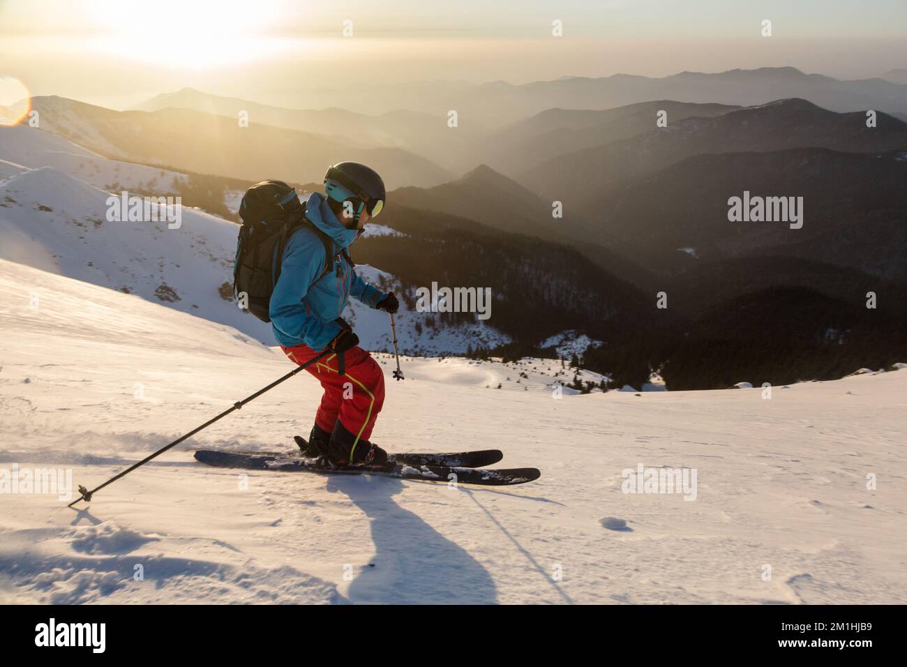Skier freerider starts descent, beautiful sunset of golden sun and ...