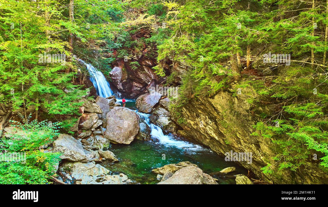 Aerial over river in rocky gorge of lush green forest with waterfall ...