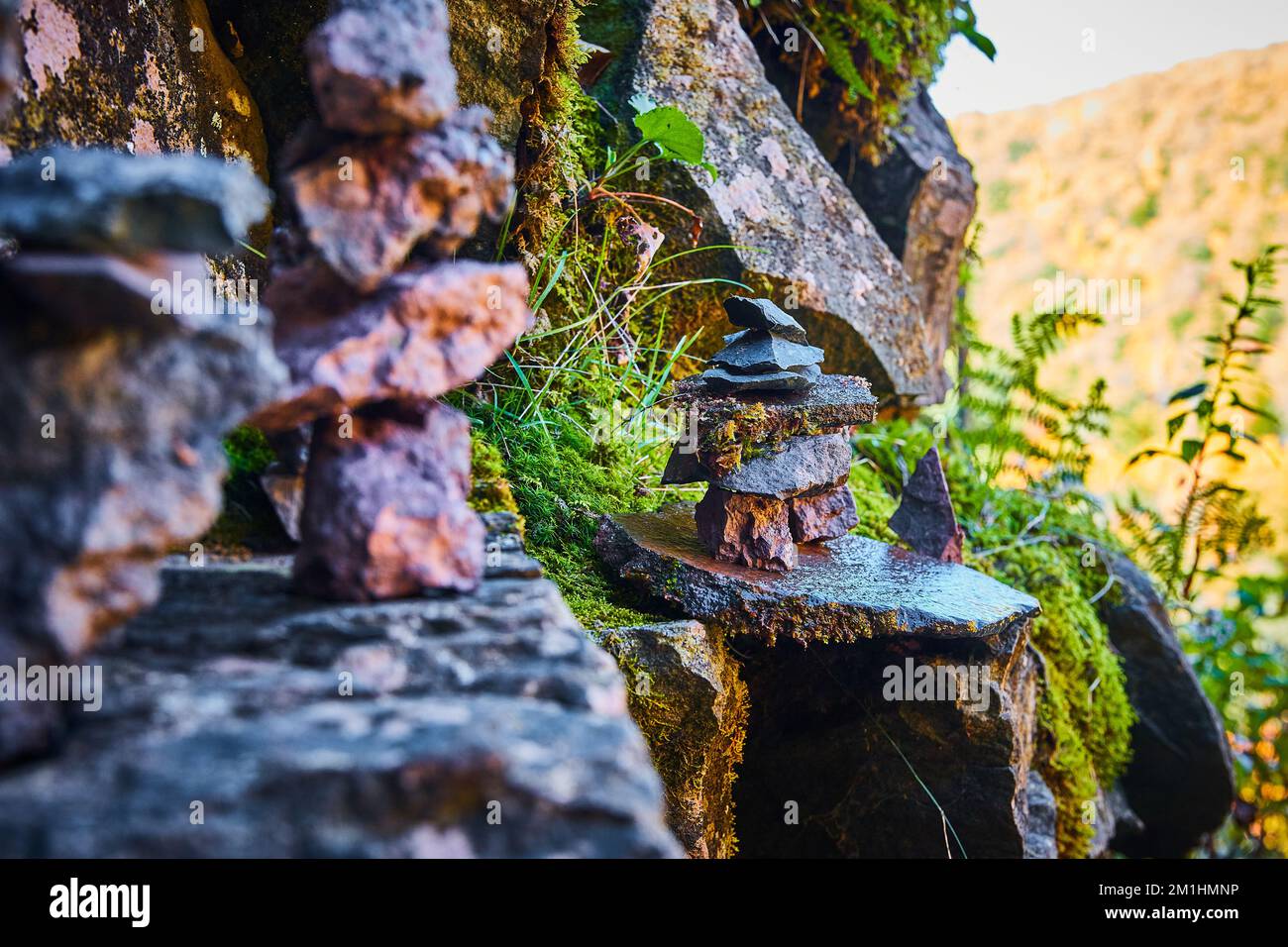 Group of small rocks stacked cairn against stone wall with moss and ...