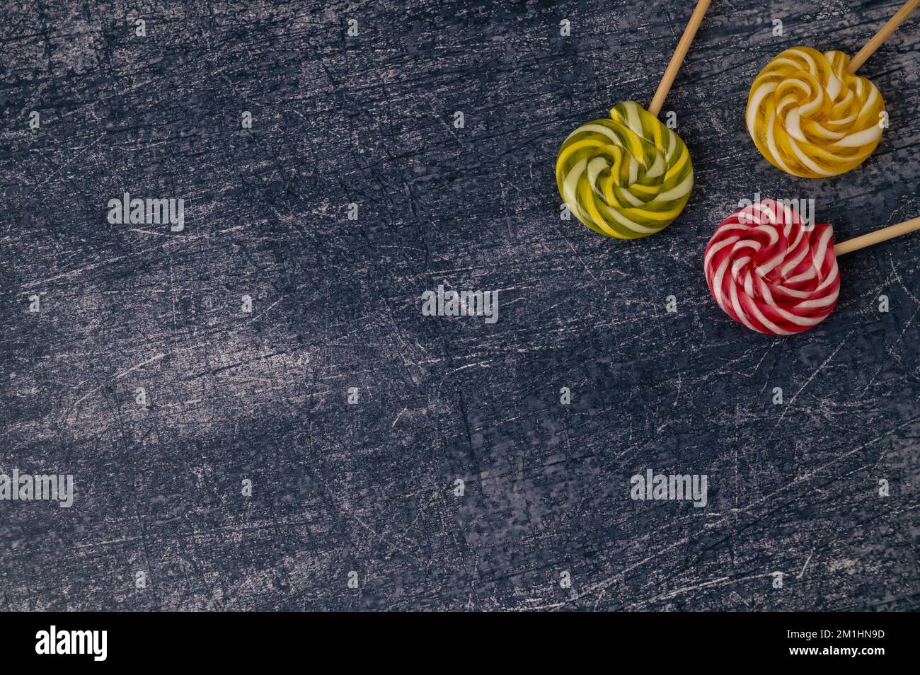 Three colored caramels on a stick in the upper corner on a dark blue ...