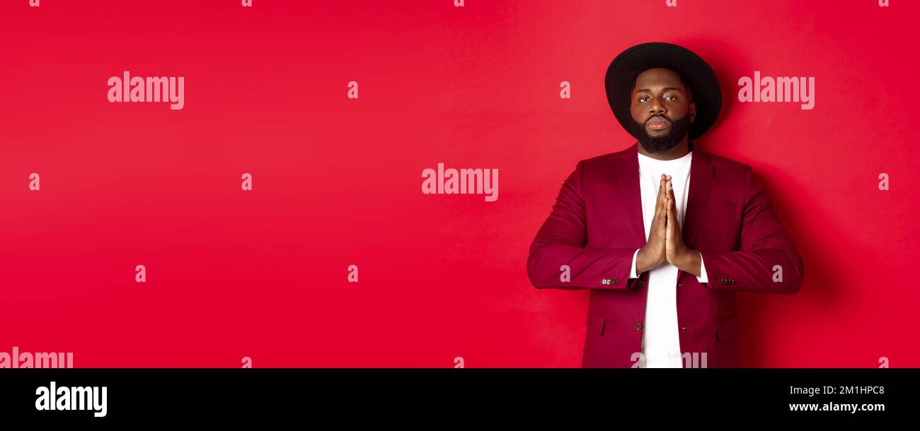 Serious african american man showing respect, holding hands together in ...