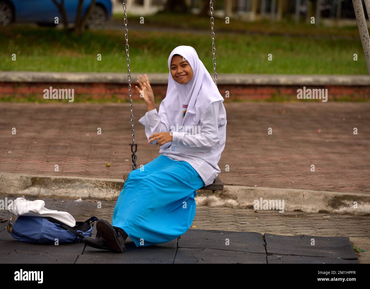 A young, indigenous Rungus girl sitting on a swing and waving in Kudat ...