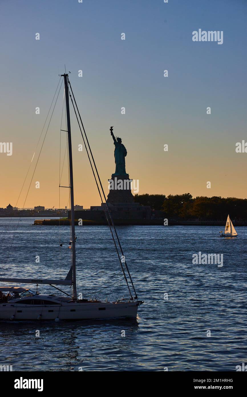Golden hour silhouette of Statue of Liberty with boats sailing past ...