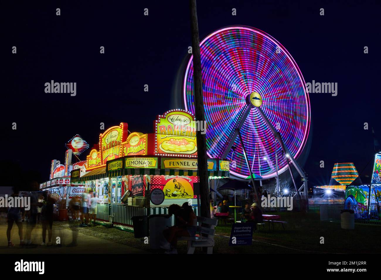 Blurred purple lights on ferris wheel by carnival food vendors at ...