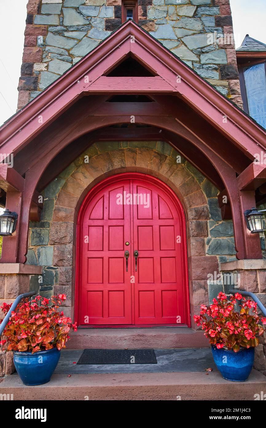 Straight on pair of red arched doors with stone wall and red plants ...