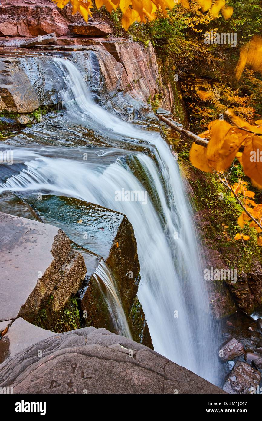 On edge of rocky cliff by huge waterfall pouring over edge with yellow ...