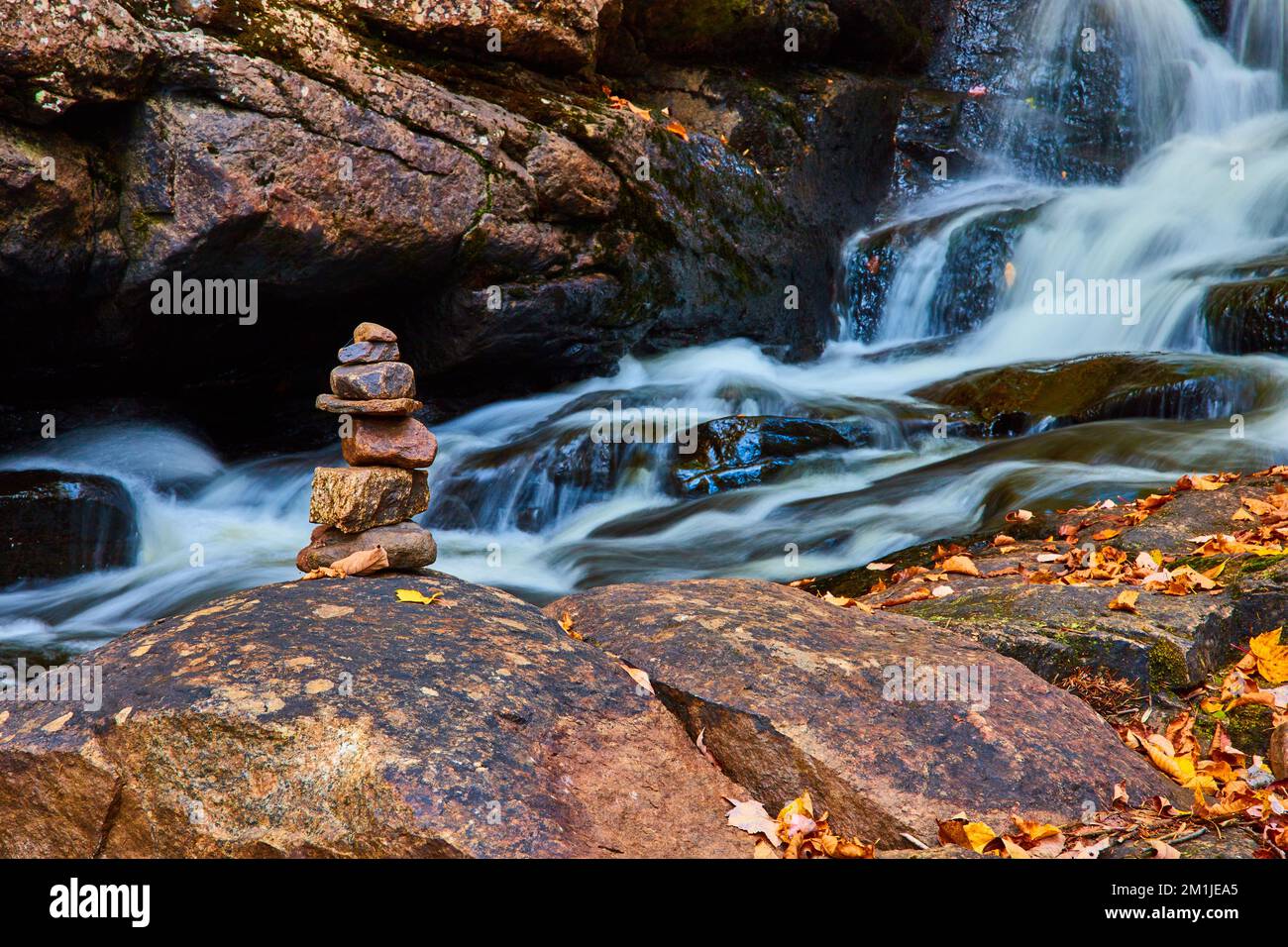Stack of rocks cairn on edge of cascading river with fall leaves Stock ...