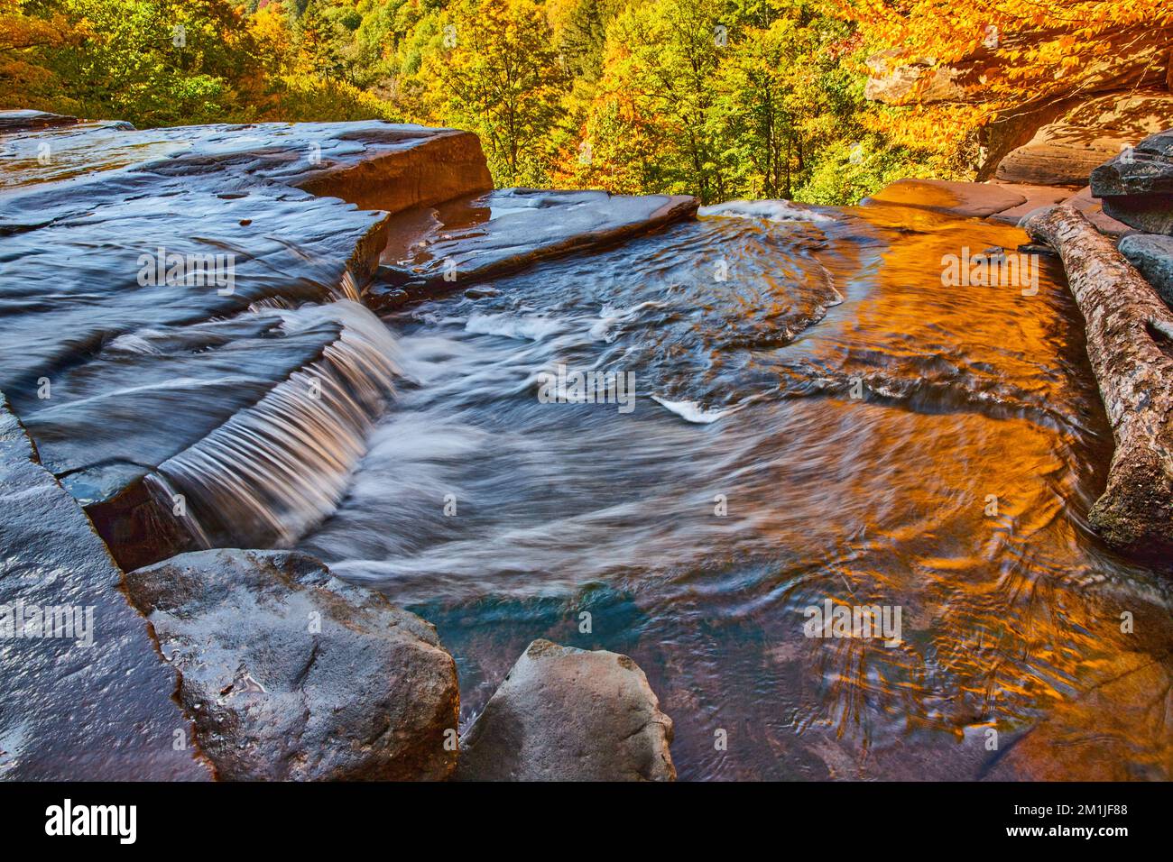Tiny waterfall over rocks leading to cliff edge and fall foliage Stock ...