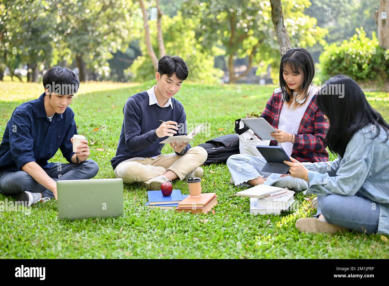 Happy young Asian college students relaxing in the campus's park, discussing and working their ...