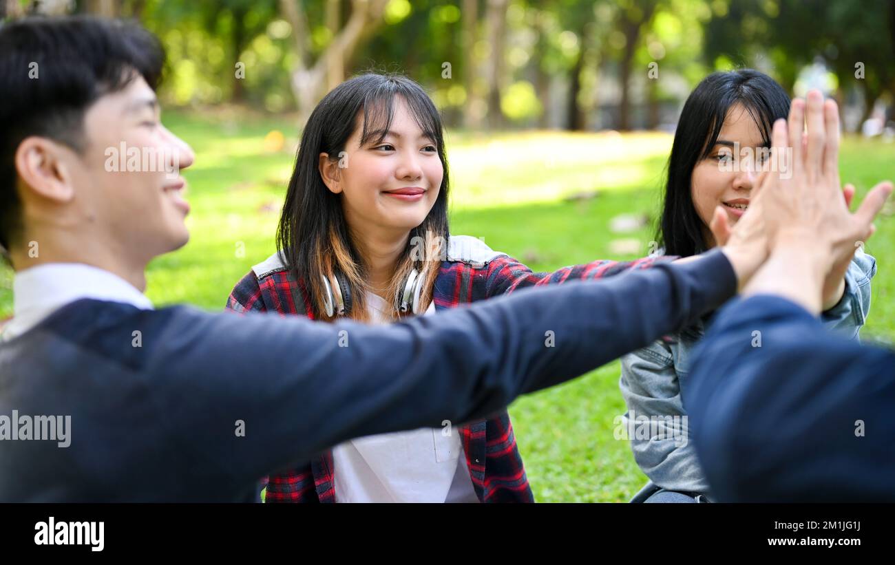 Cheerful young Asian friends putting hands together as a teamwork ...