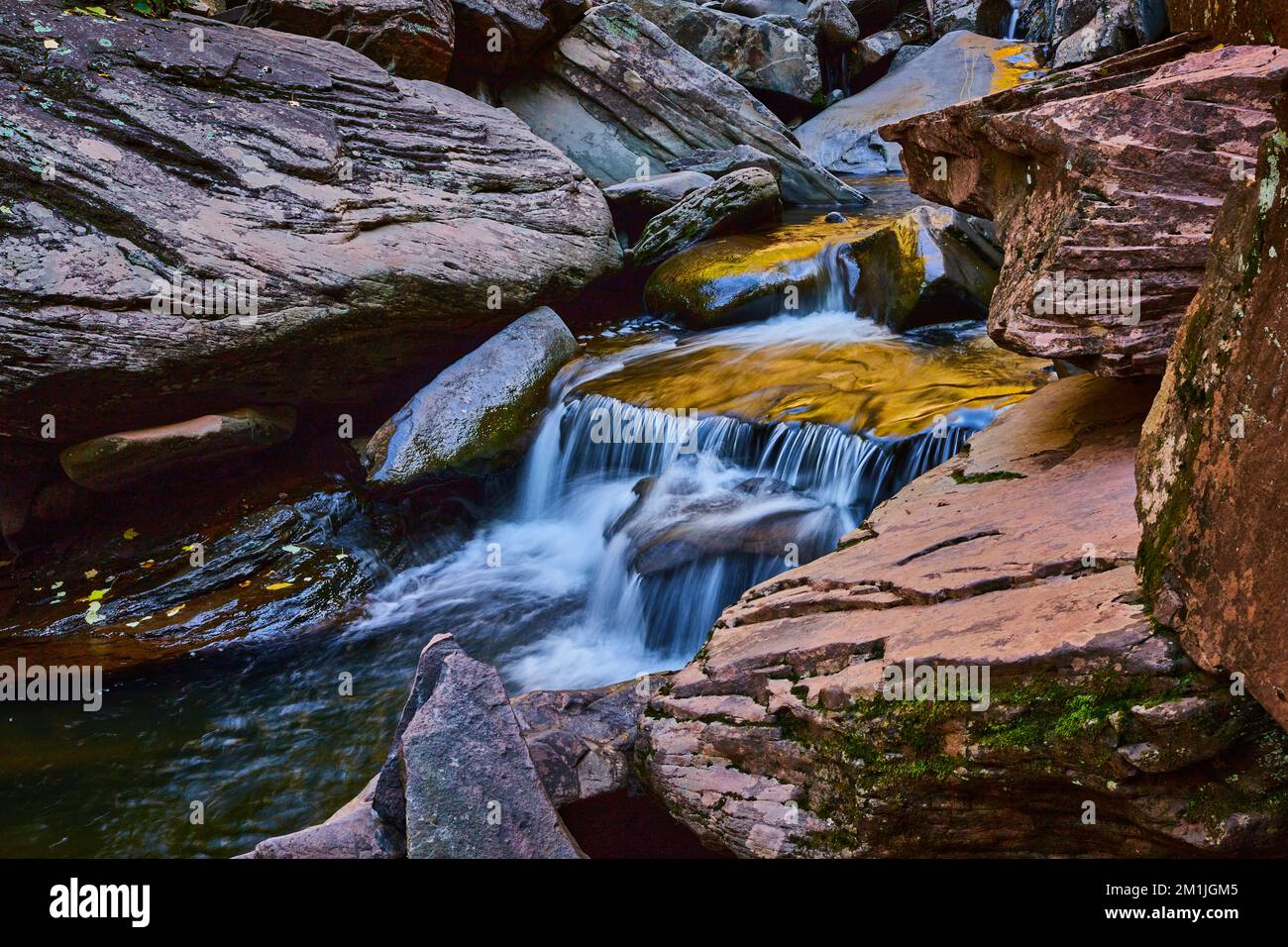 Up close to small cascading waterfall surrounded by lichen and boulders ...